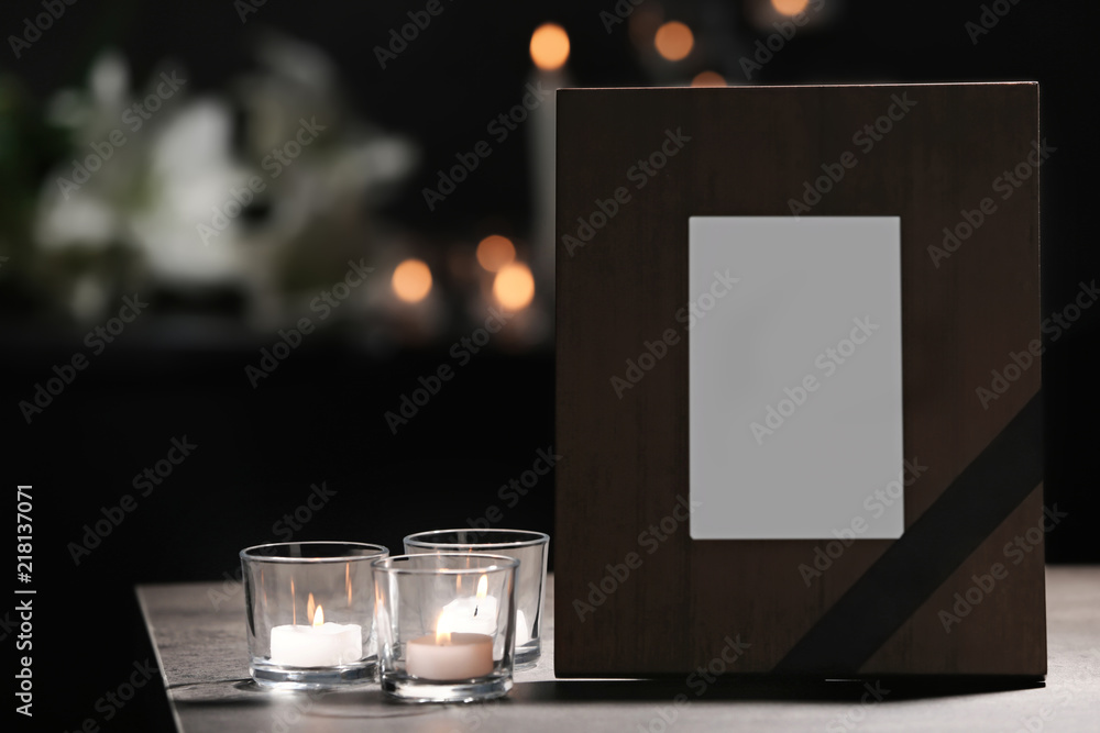 Funeral photo frame with black ribbon and burning candles on table in ...