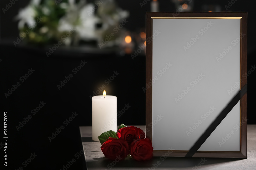 Funeral photo frame with black ribbon, roses and burning candle on ...