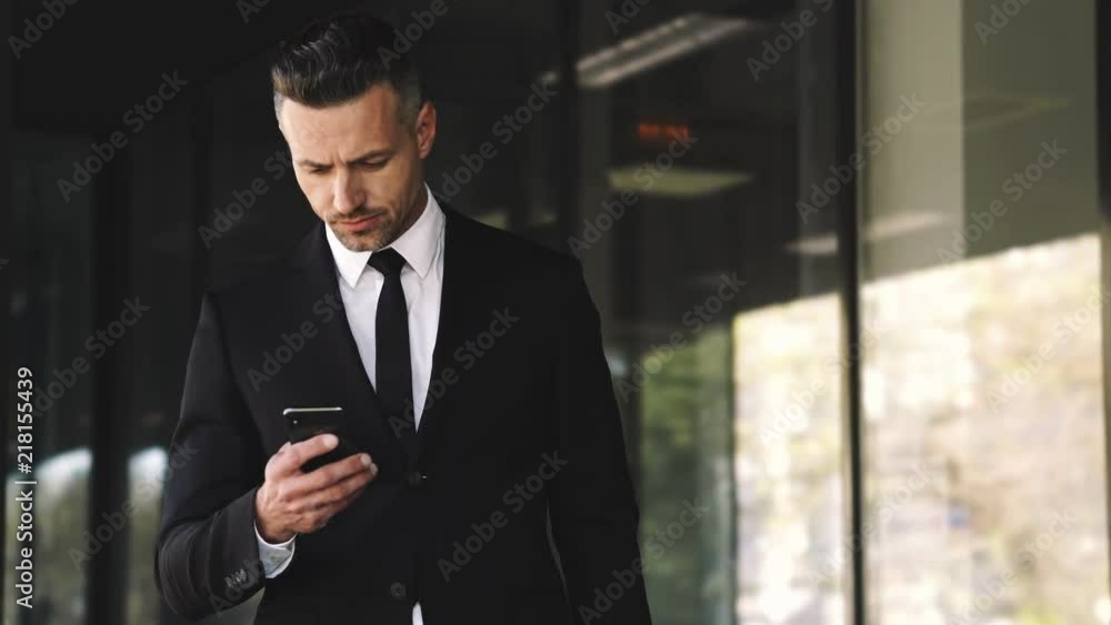Serious business man dressed in suit using smartphone while waitng ...