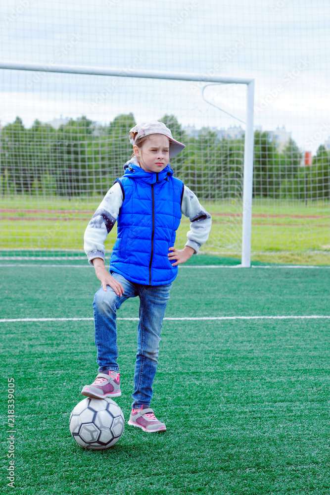Little girl is standing on the football field in front of a gate ...