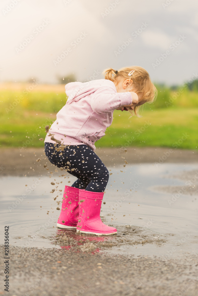 Small girl playing in puddle and splashing water her wellies. Stock ...