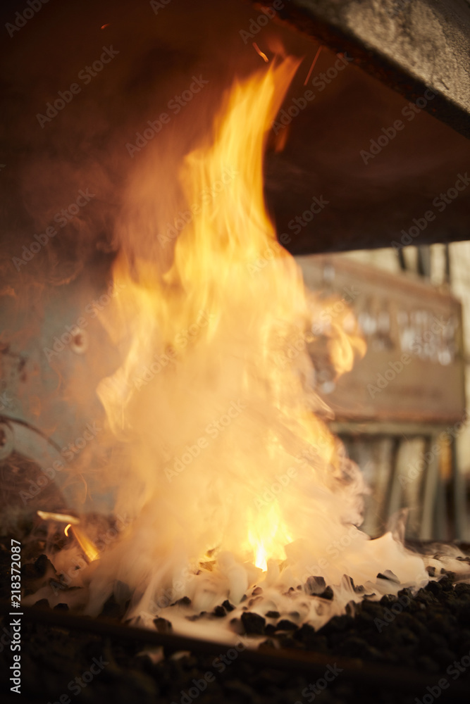 Flames and smoke billowing from a forge fire in a metal workshop. Stock ...