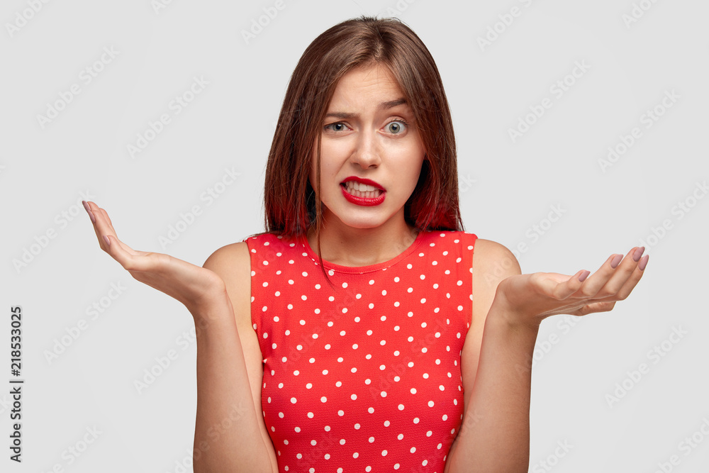 Puzzled unaware brunette female dressed in stylish clothes, wears red ...