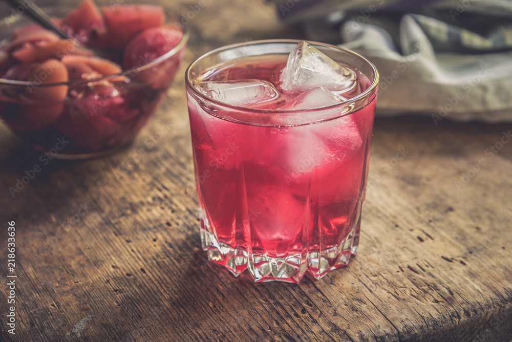 Red fruit drink with ice on an old rustic table with a cup of apples in ...