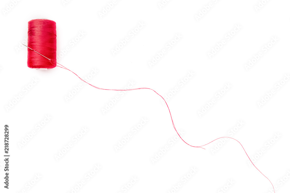Overhead photo of a needle with a red thread and a spool on a white ...