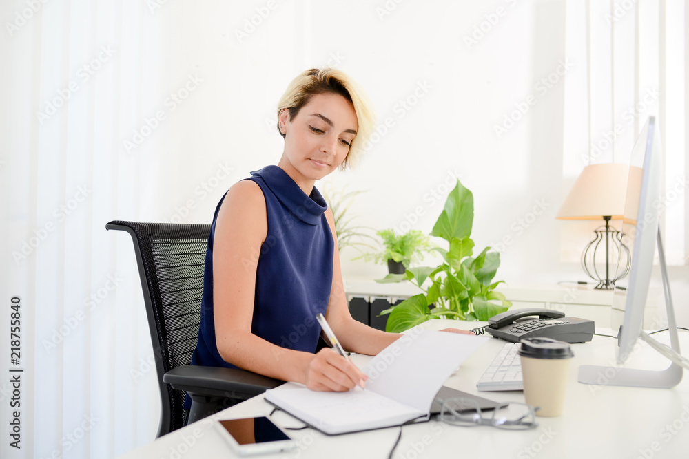 beautiful young business woman working at desk in a white and bright ...