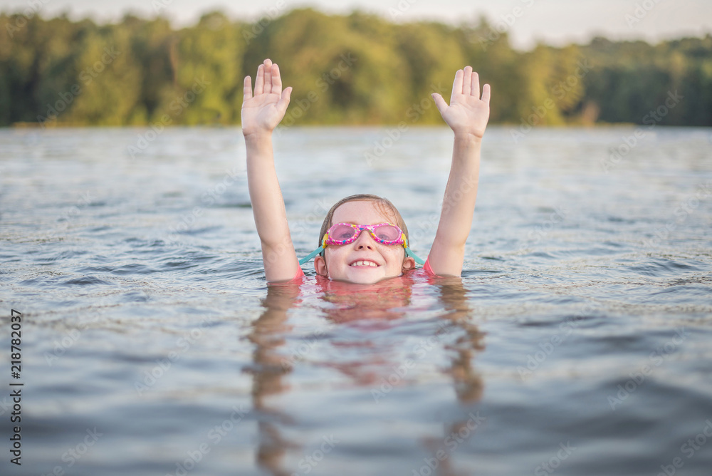 Foto de Young girl swimming in lake wearing goggles raising hands over ...