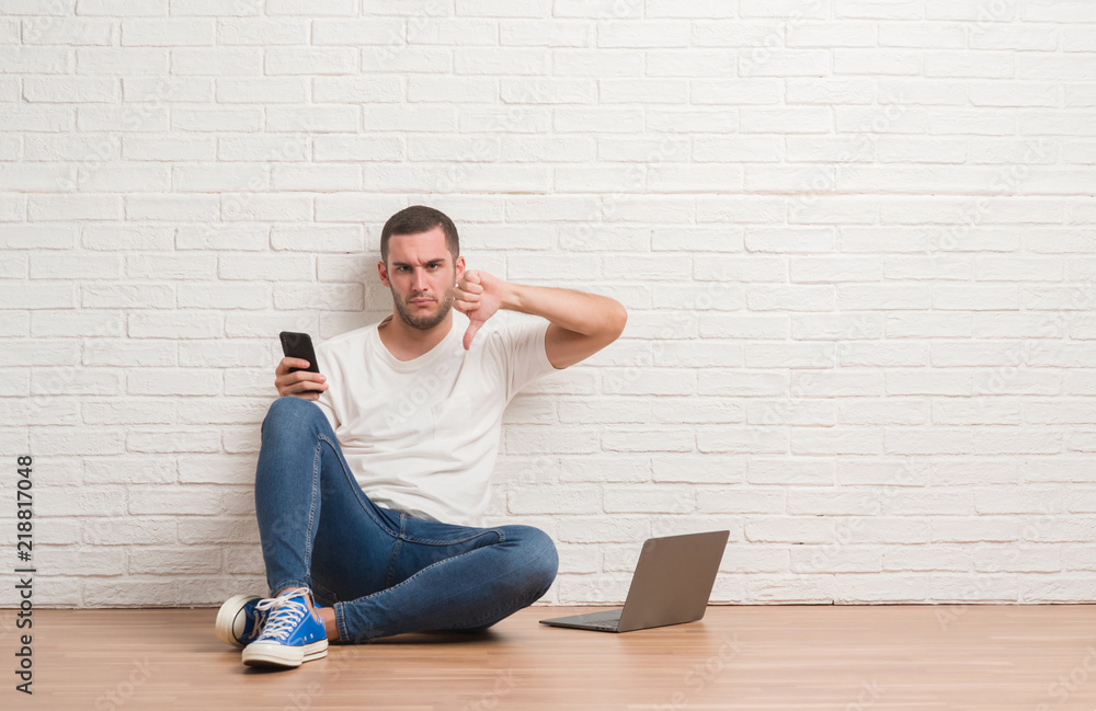 Young caucasian man sitting over white brick wall using computer laptop ...
