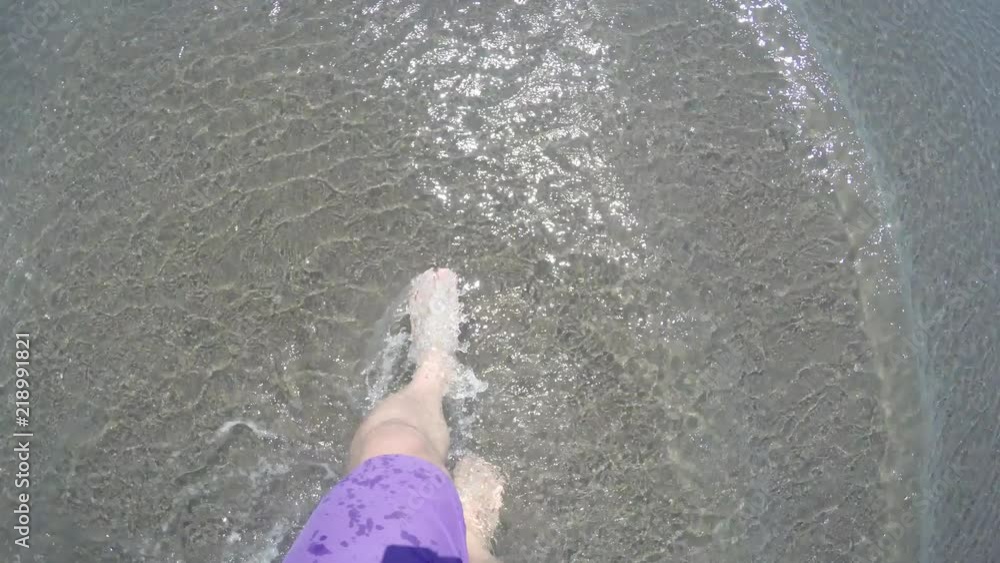 Man's feet walking through shallow water at the beach. Entering the ...
