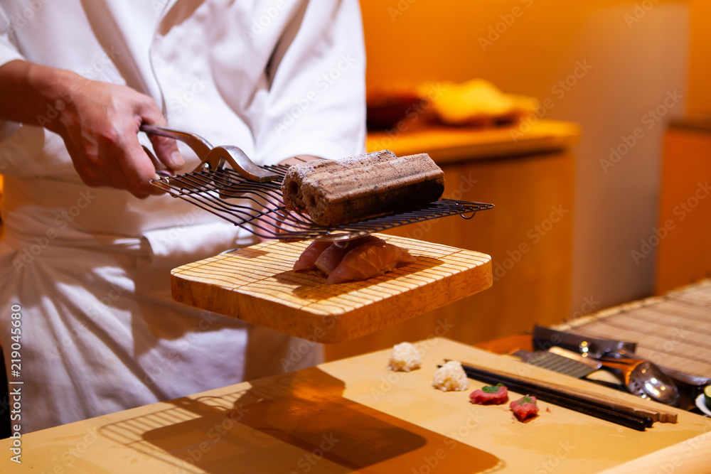 Professional sushi chef using red hot charcoal to aburi or flame seared ...