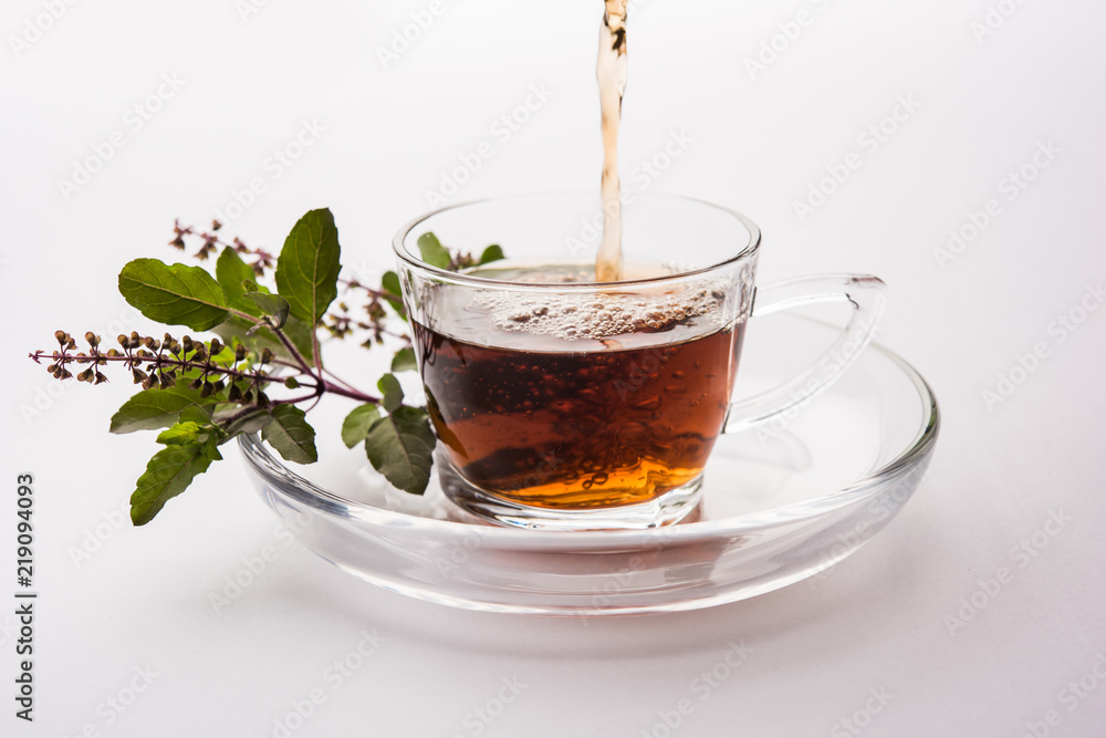 pouring Holy Basil or Tulsi Tea in transparent glass cup with saucer ...
