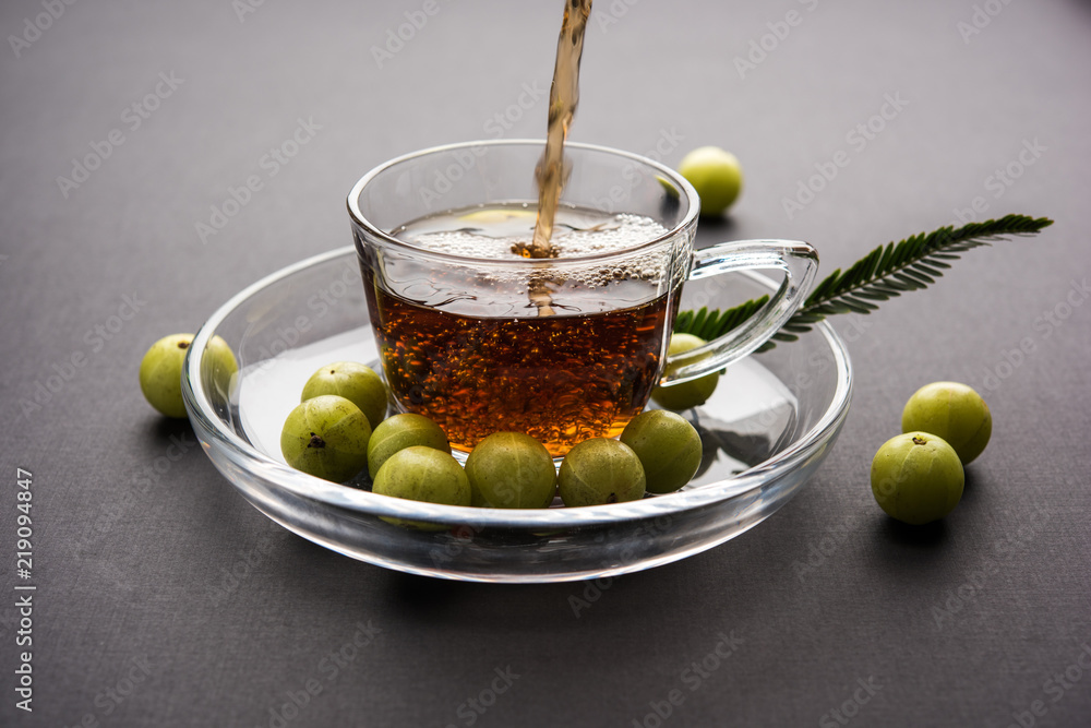 pouring amla Tea or Avla Chai in transparent glass cup with saucer over ...