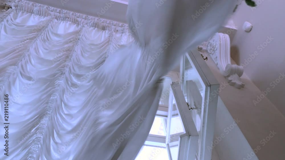 A mystical white textured curtain is blown by the wind from the window ...