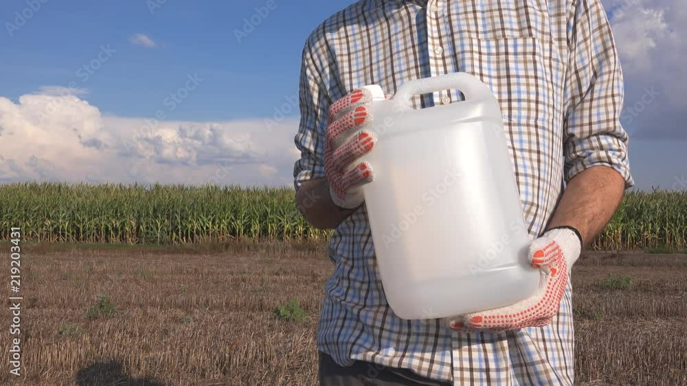 Farmer holding pesticide chemical jug in cornfield. Blank unlabelled ...