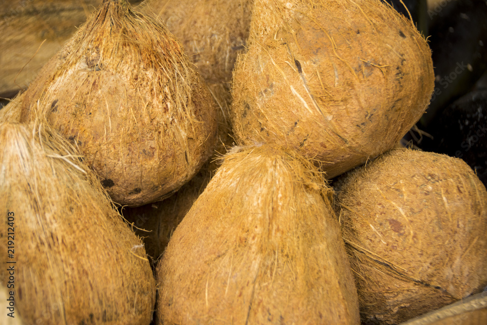 A close-up photo of a pile of coconuts on a brown wooden table. The ...