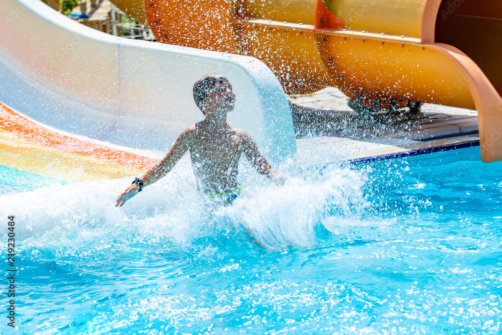 A happy boy on water slide in a swimming pool having fun during summer ...