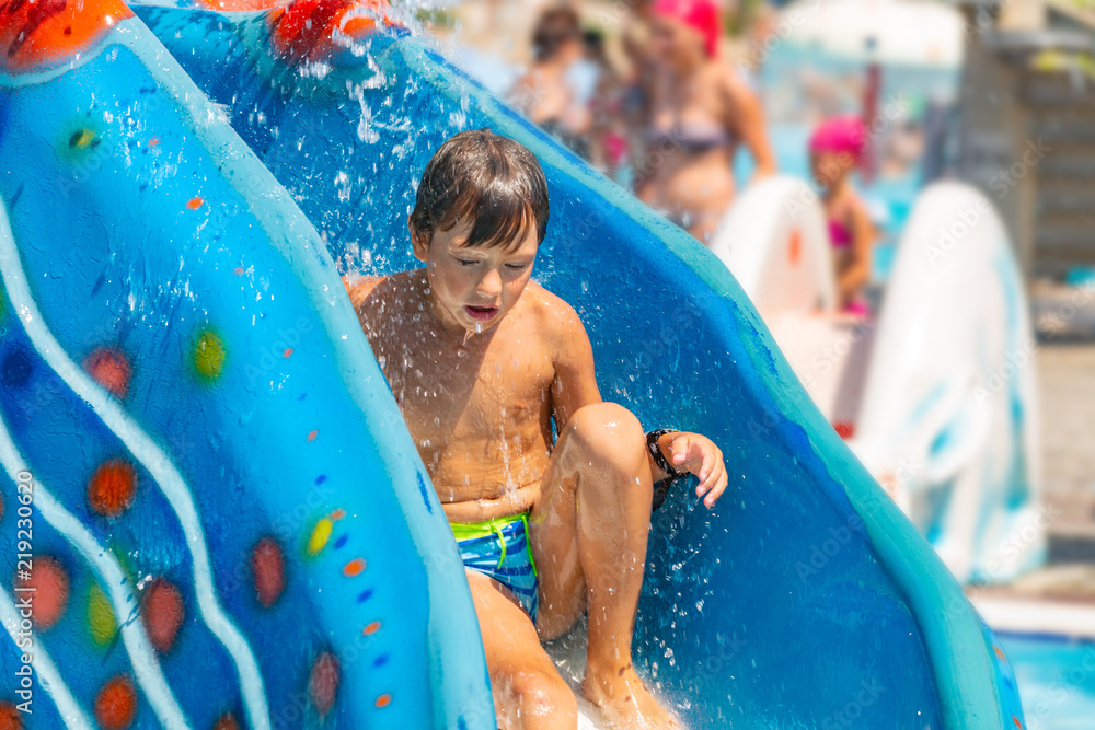 A happy boy on water slide in a swimming pool having fun during summer ...