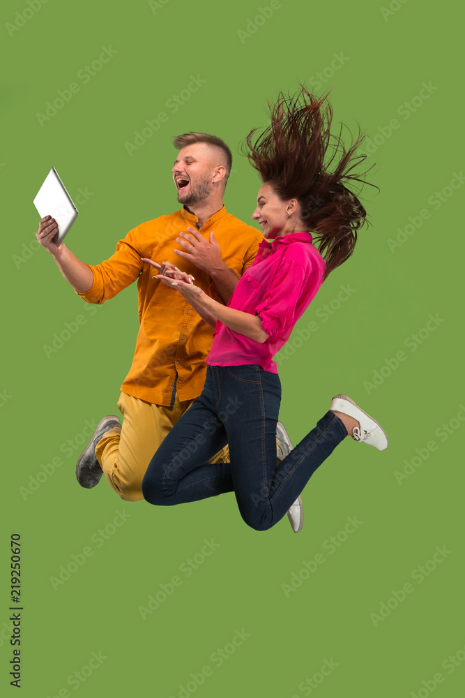 Jump of young couple over green studio background using laptop or ...