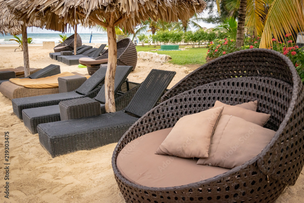 Sun beds/ lounge chairs and straw thatch roof umbrellas by the beach in ...