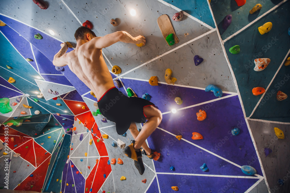 Close-up of male climber on sport climbing gym wall holding onto ledges ...