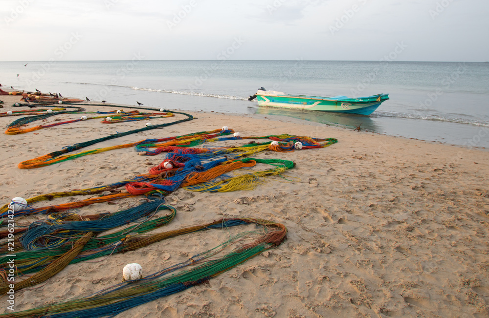 Multi-colored fishing nets drying in the sun next to small fishing boat ...