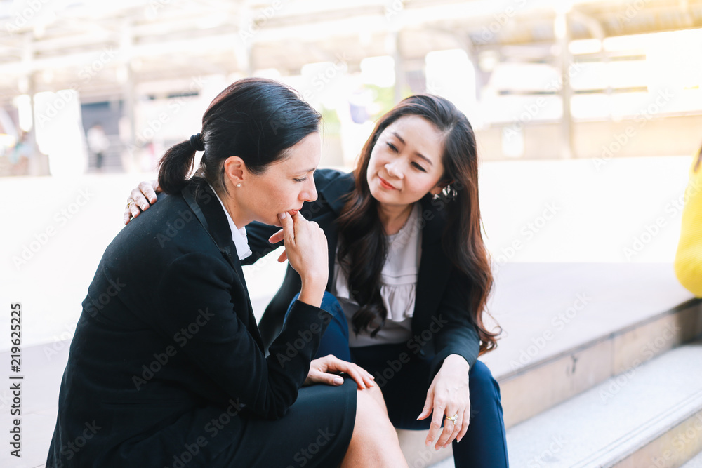 Businesswomen sit on the steps in the city, one of whom is comforting ...