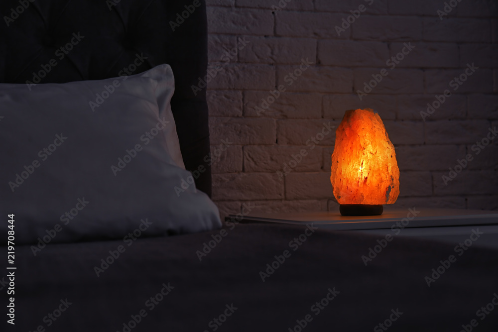 Himalayan salt lamp glowing on bedside table in dark room Stock Photo ...