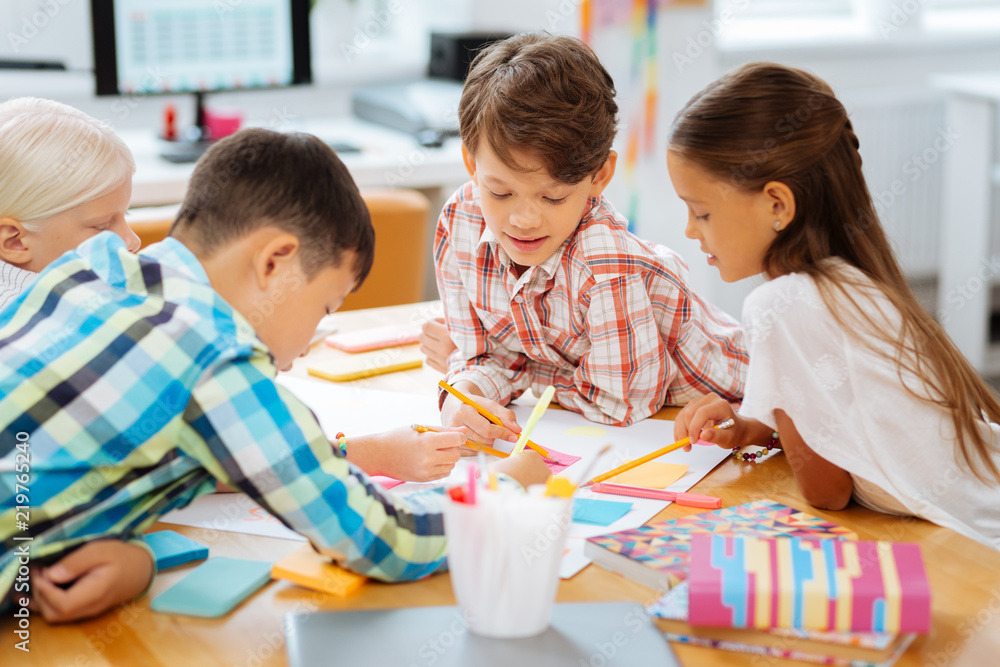 Involved. Joyful classmates drawing pictures while being in a classroom ...