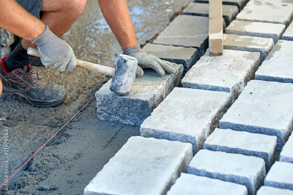 A workman's gloved hands use a hammer to place stone pavers. Worker ...
