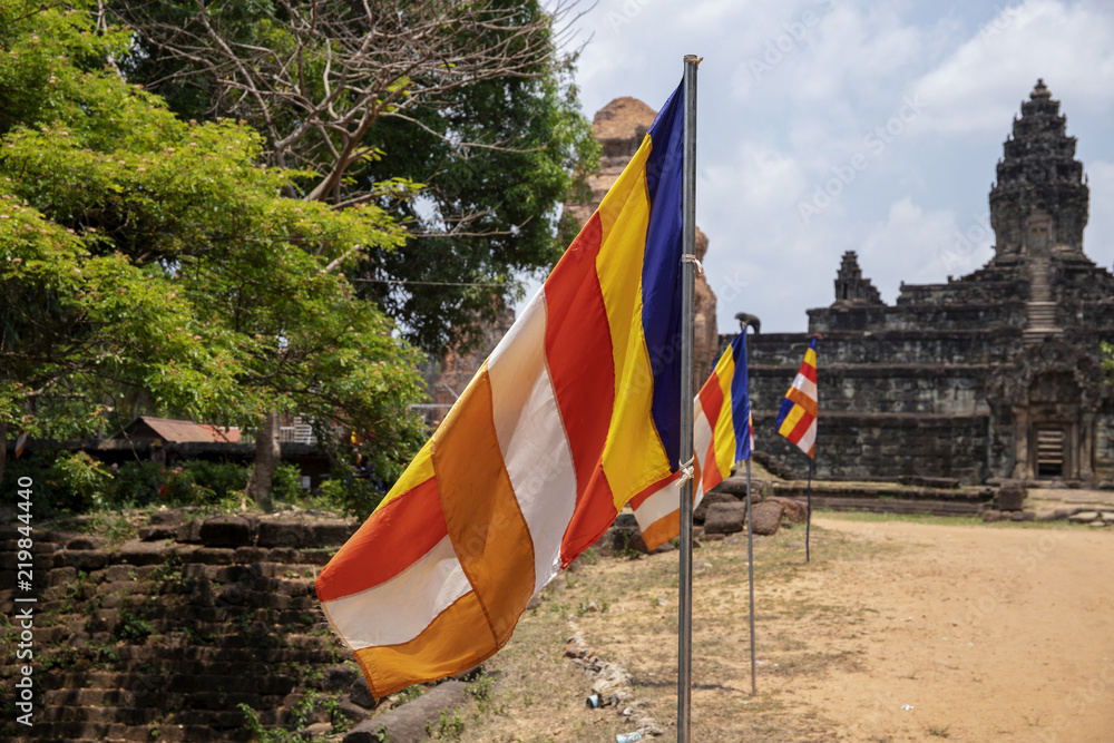 Striped buddhist flag near ancient stone temple, Roluos temple complex ...