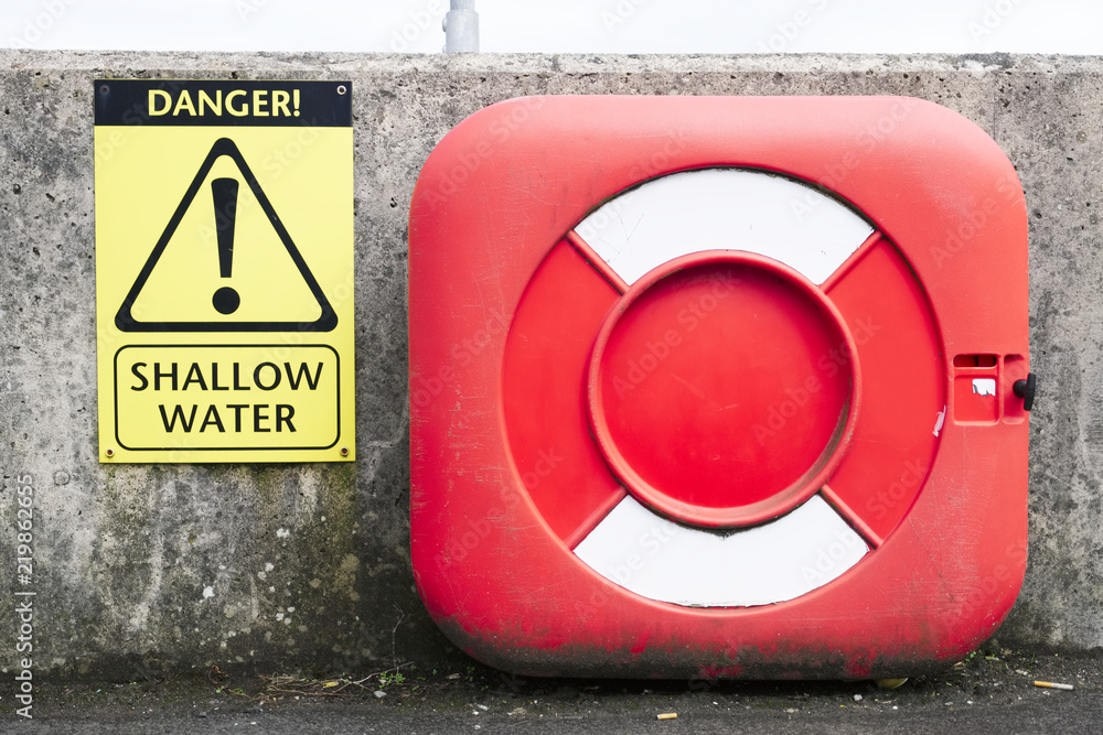 Shallow water sign and red life safety buoy at harbour wall Stock Photo ...