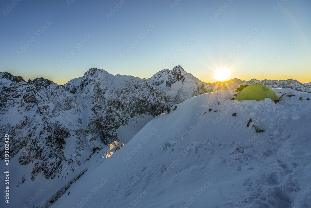 Yellow tent pitched up on a summit of a high alpine peak. Winter ...