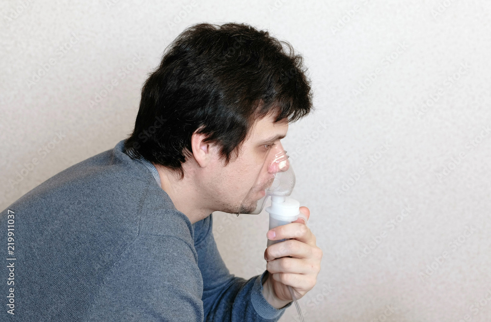 Use nebulizer and inhaler for the treatment. Young man inhaling through ...