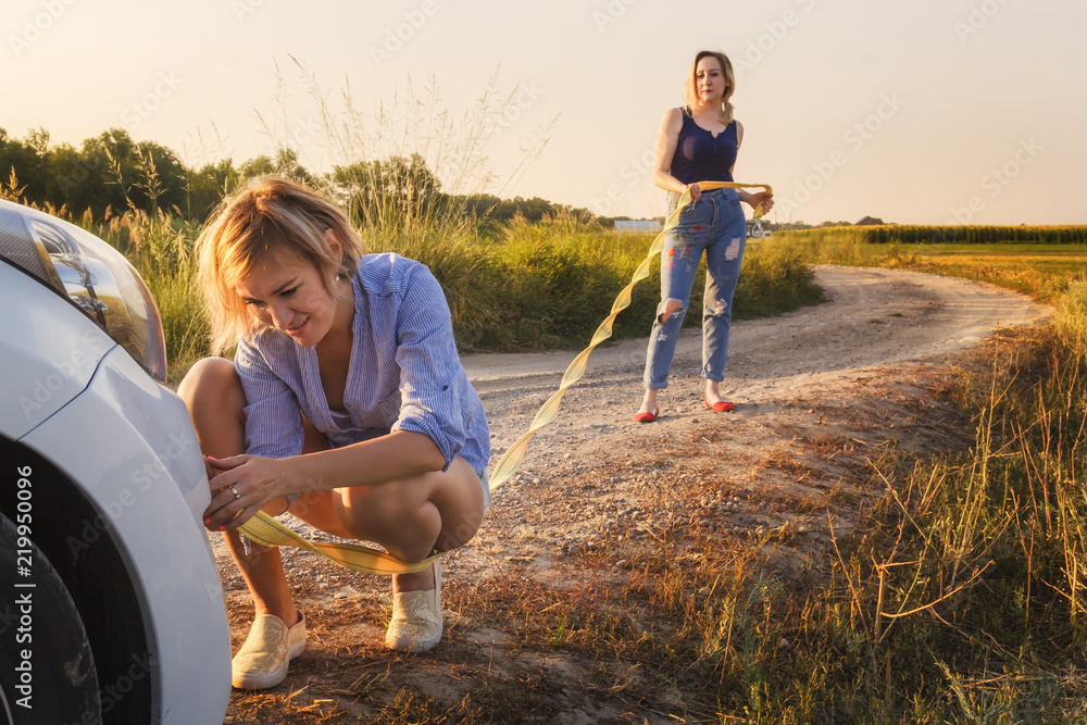 Two girls catch a tow rope on a broken car on a rural road in the rays ...
