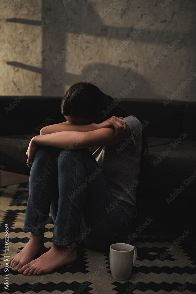 emotional crying woman hugging her knees while sitting on floor at sofa ...