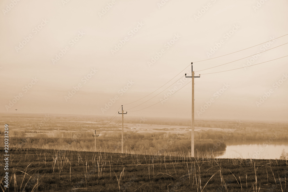 Atmospheric landscape with power lines in field on background of river ...