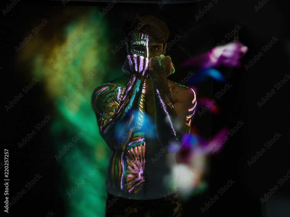 Young man painted in fluorescent paint on face and muscular torso, in ...