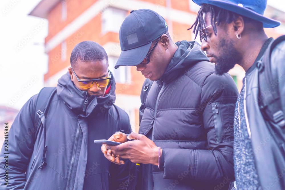 three young black men outdoor using smart phone - wifi technology ...