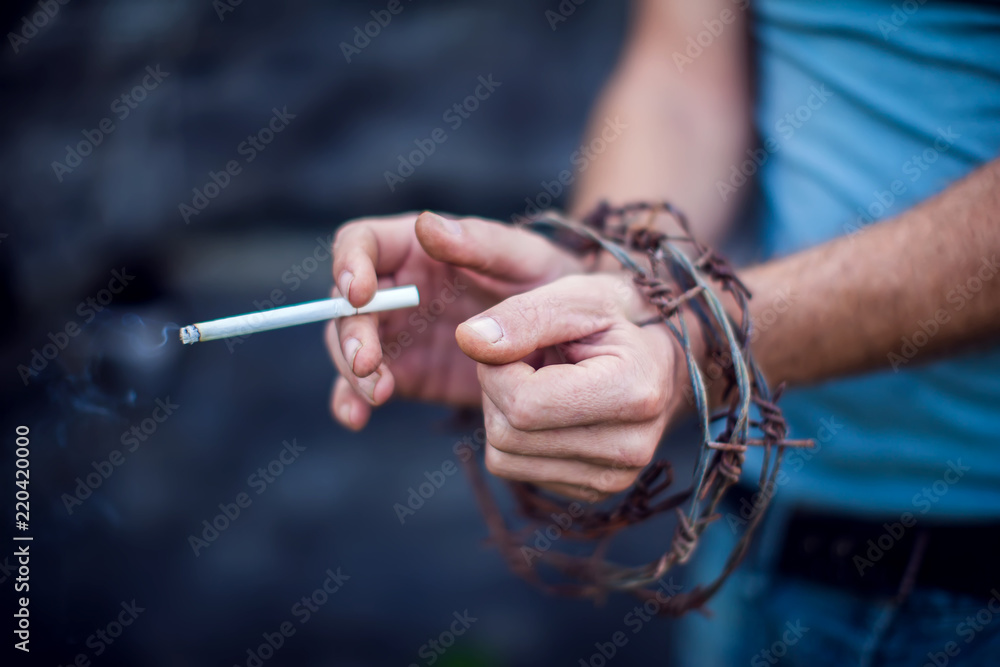 Cigaret in hands with barbed wire on a dramatic background. Concept of ...