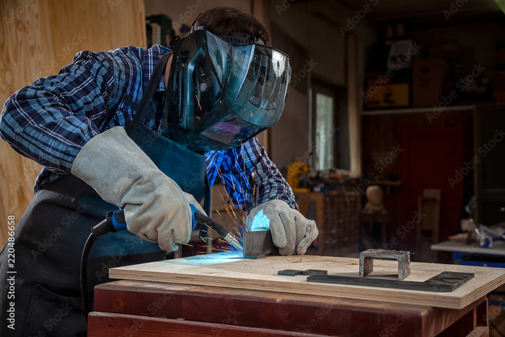 Strong man welder in work clothes hard working and welds with a welding ...