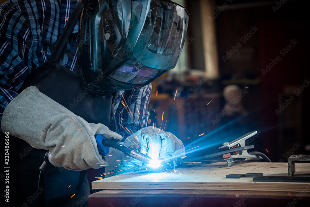 Strong man welder in work clothes hard working and welds with a welding ...