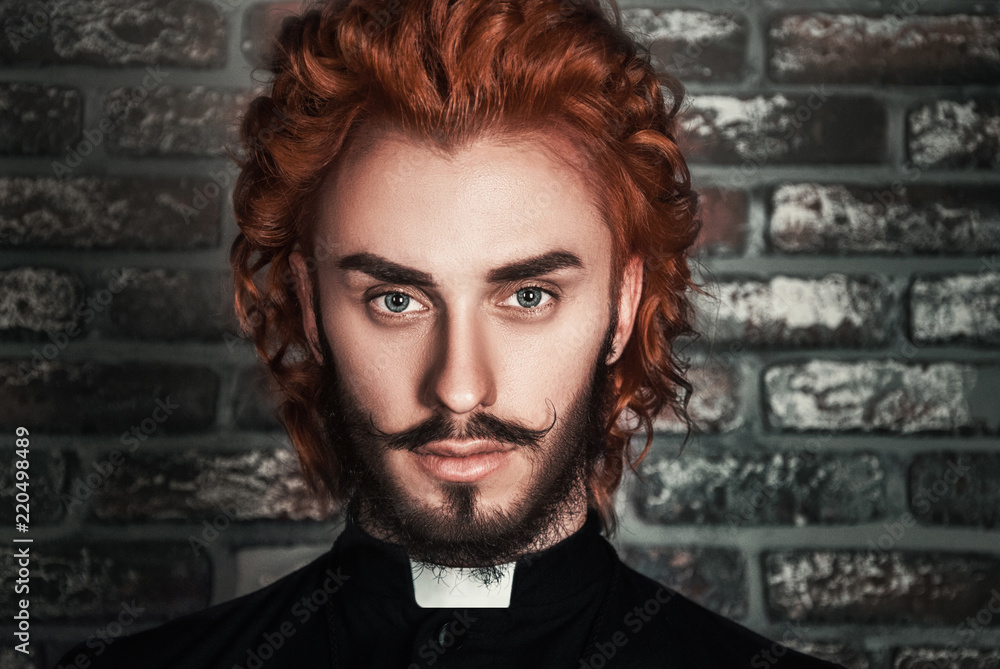 Close-up portrait of young red-haired man wearing priest garment, with ...