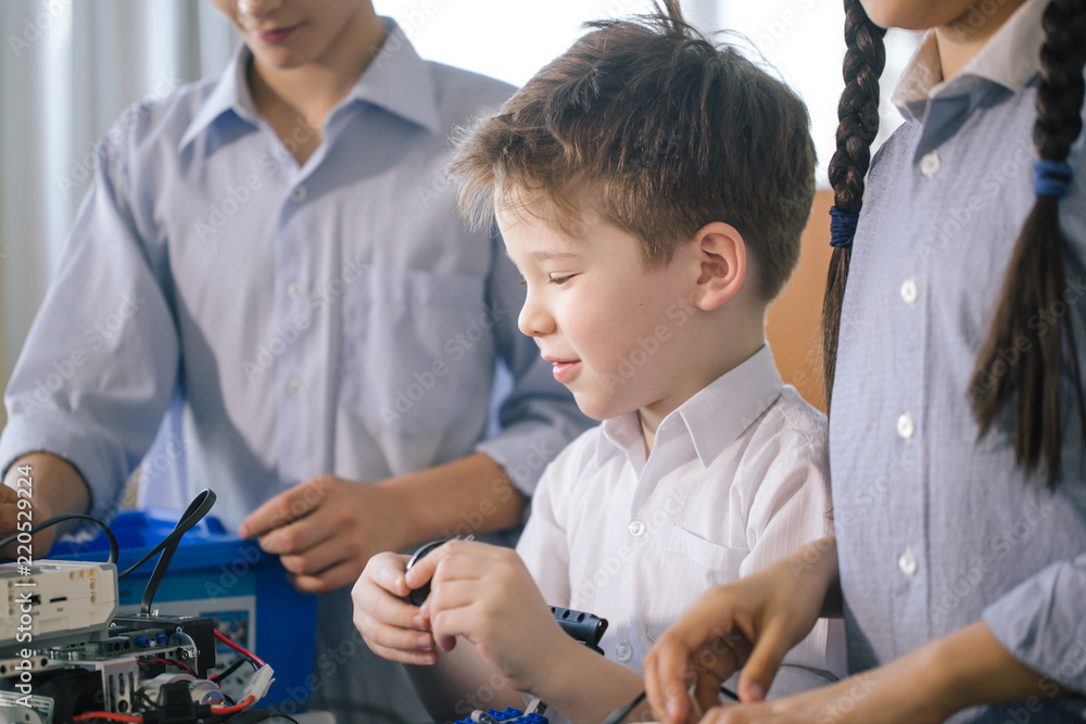 Fair haired cheerful little boy making a robot from metal parts and ...