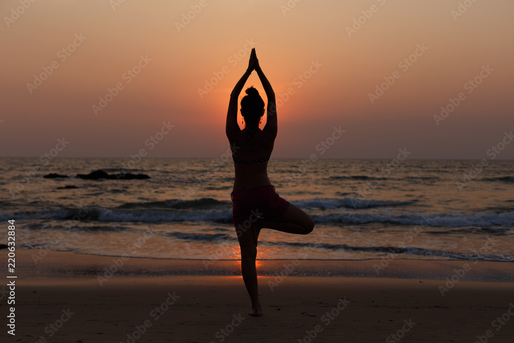 Young slender girl with her back doing yoga at sunset on the beach ...