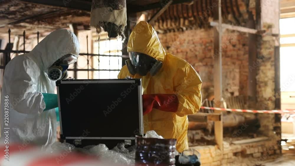 Two men wearing airtight suits standing near black suitcase with ...
