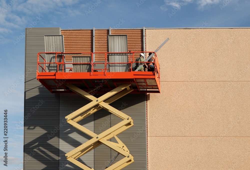 Workers on a cherry picker refurbish the facade of a building by ...