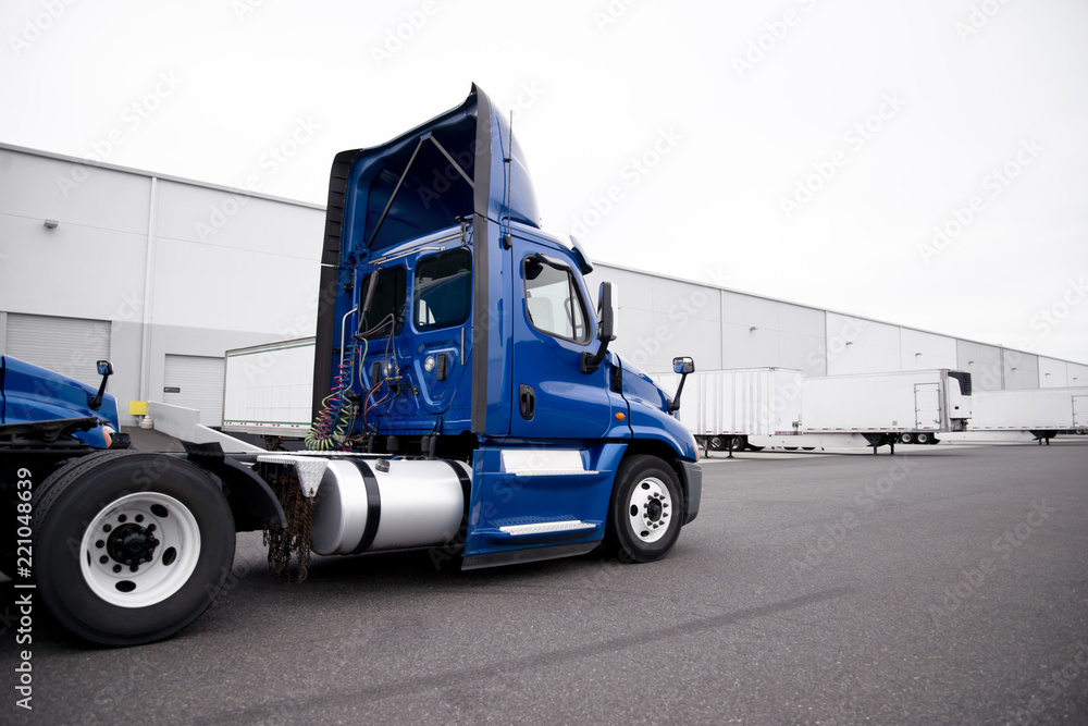 Big rig day cab blue semi truck driving to warehouse dock for pick up ...