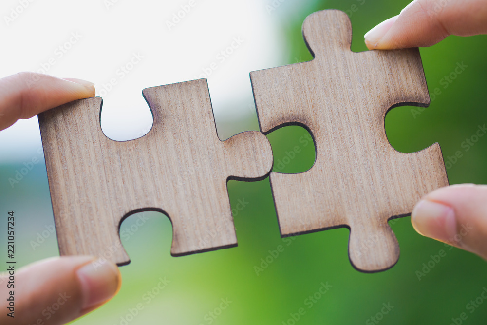Two hands trying to connect couple puzzle piece with green background ...