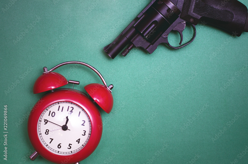 Red alarm clock and handgun isolated on green background. The waste of ...