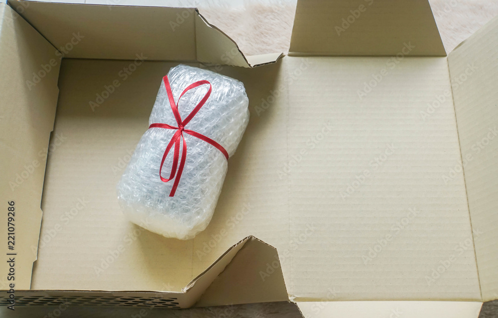 goods wrapped with bubble sheet and red ribbon put into carton package ...